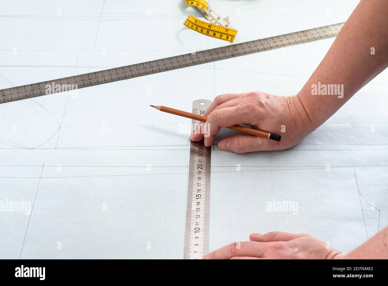 designer's hands with pencil and rulers on pattern layout of dress ...