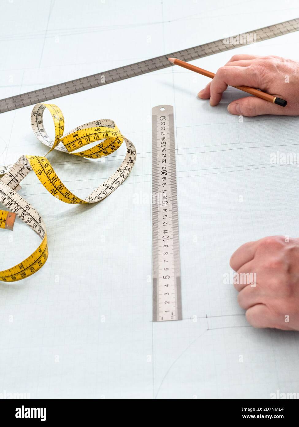 tailor's hands , measuring tape, rulers and pencil on pattern layout of ...