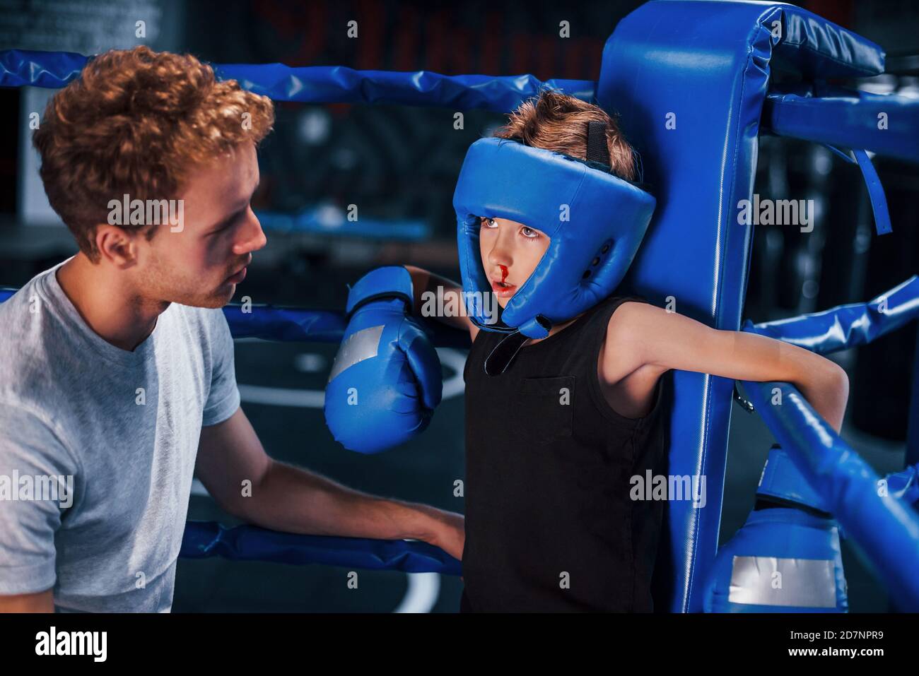 Young boxing coach is helping little boy in protective wear on the ring ...