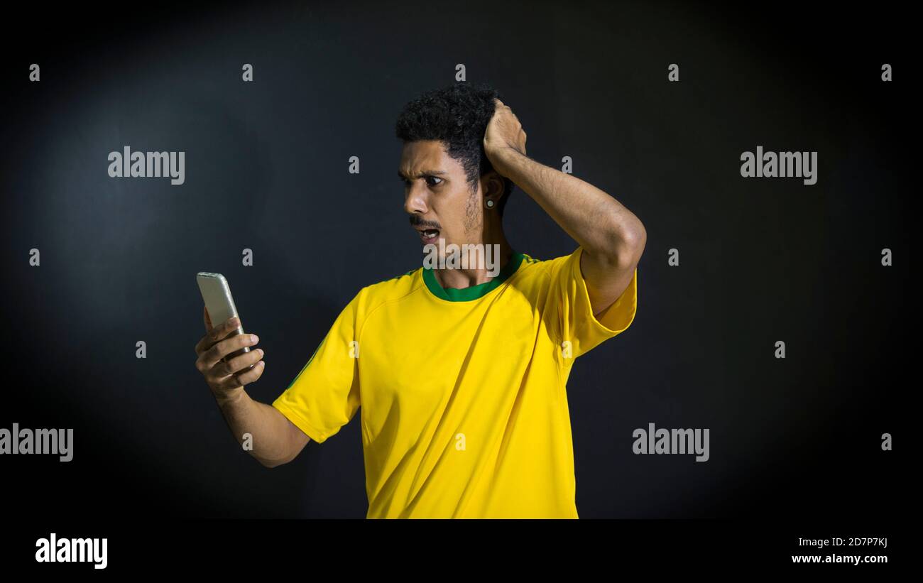 Male athlete or fan in yellow uniform looking cell phone on black ...