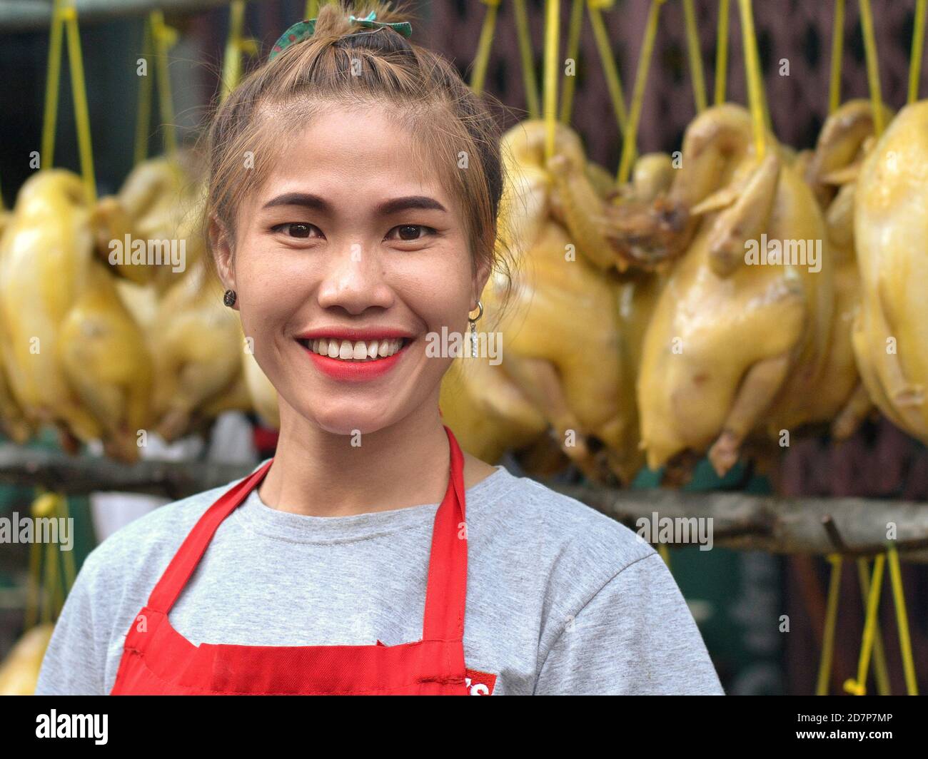Young Thai chef / cook smiles in front of a row of hanging deep-fried ...