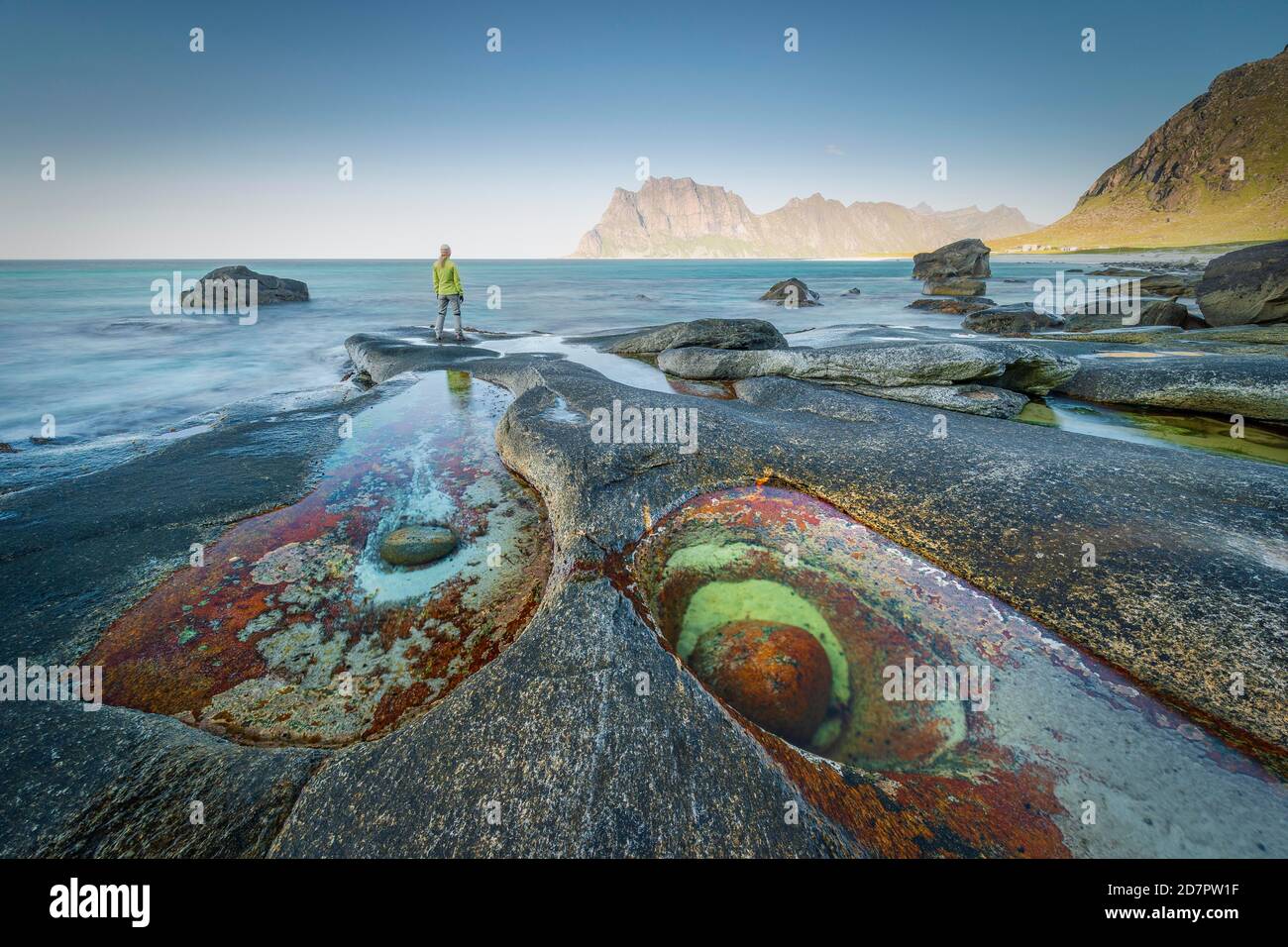 Woman standing on rocks on the beach, in front tide pool with formation ...