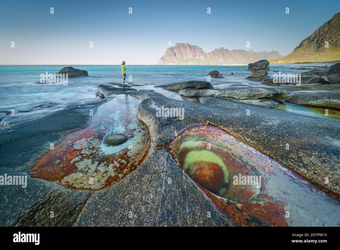 Woman standing on rocks on the beach, in front tide pool with formation ...