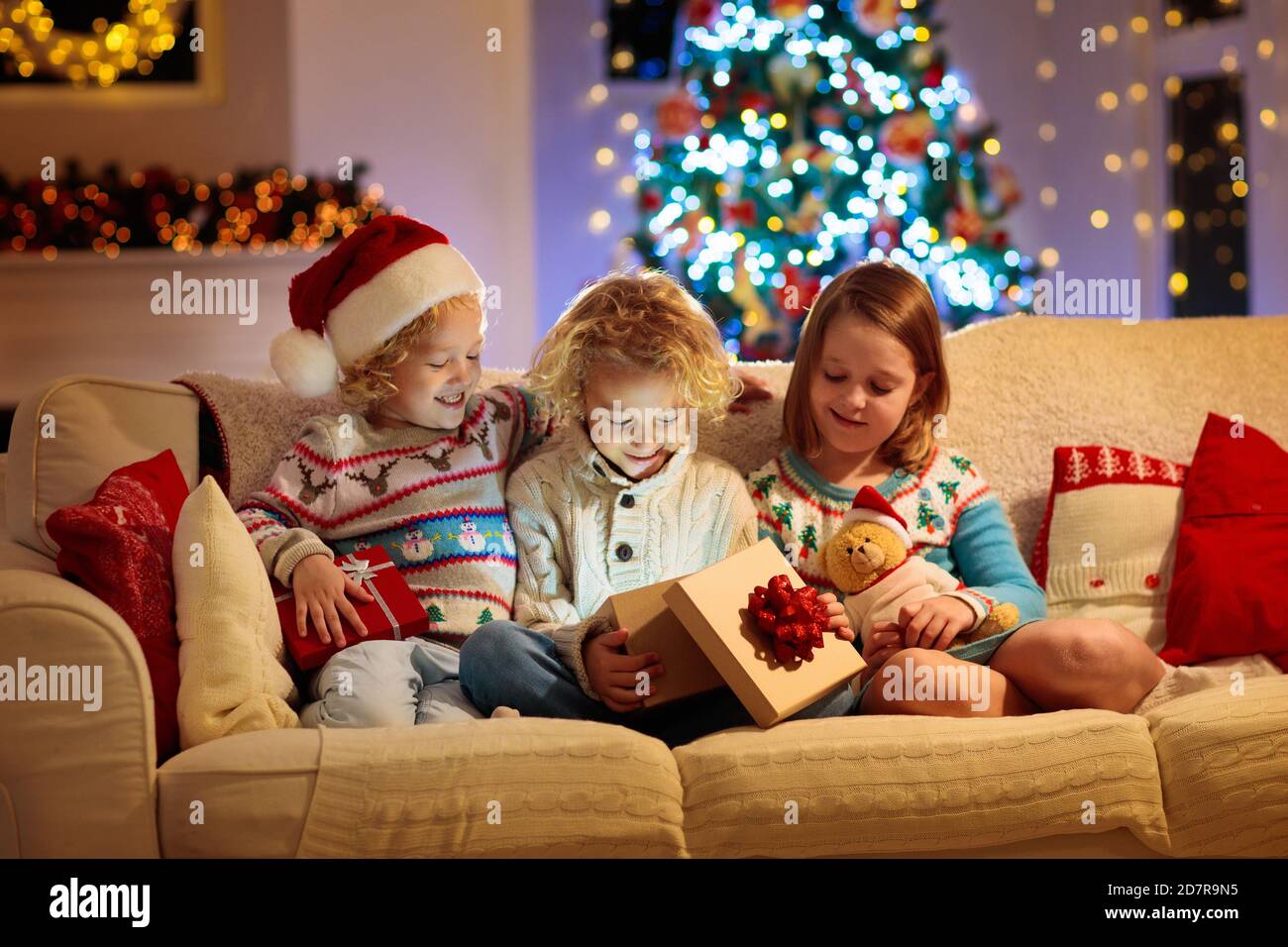 Children at Christmas tree and fireplace on Xmas eve. Family with kids ...