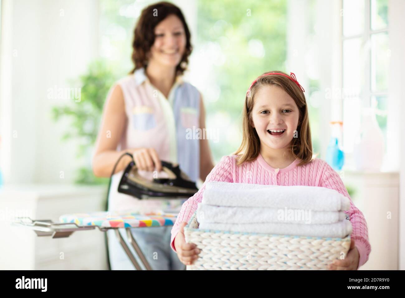 Woman and child ironing clothes. Mother and daughter folding clothes at ...
