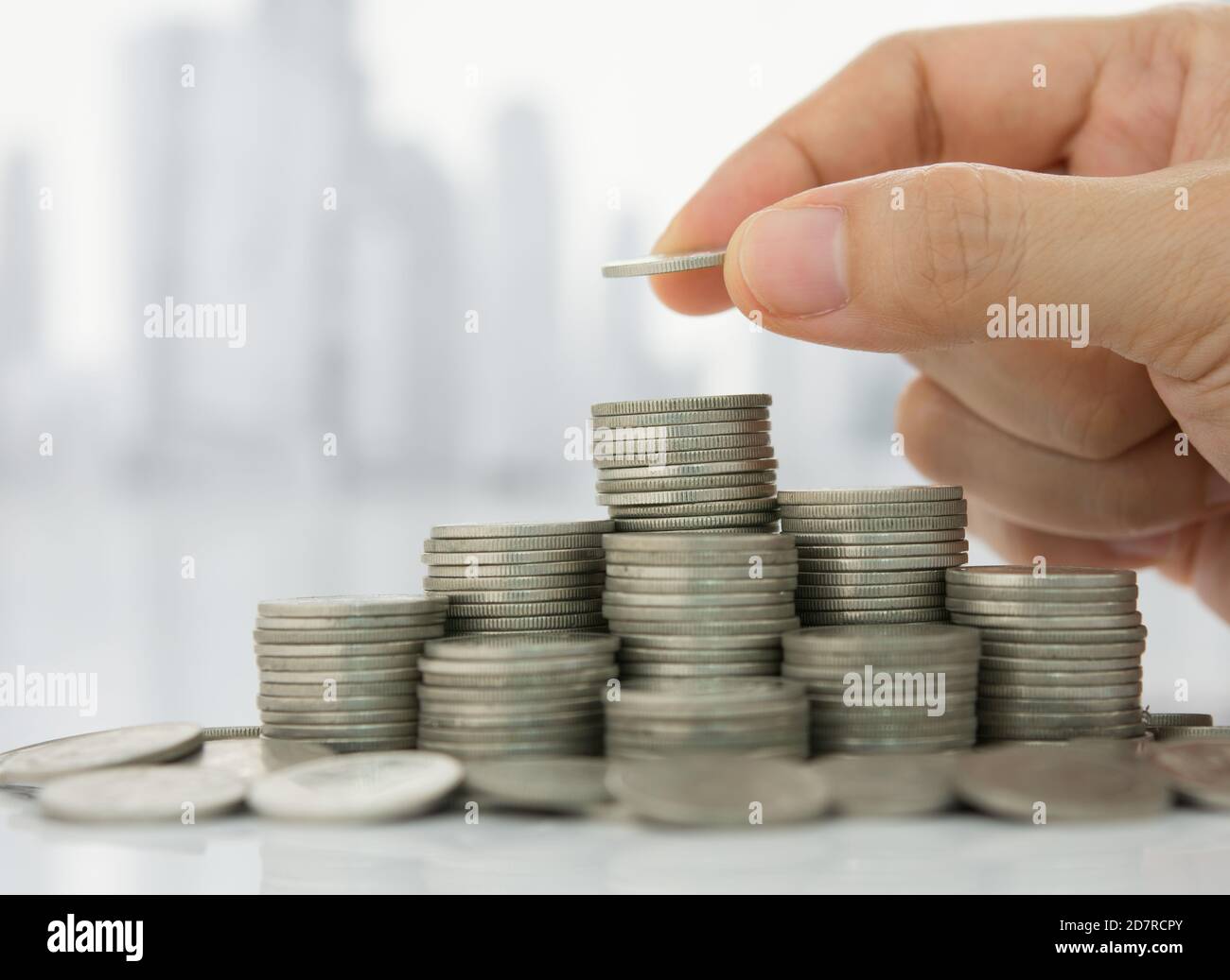 Hand putting coin on coins stack with city in background. Savings ...