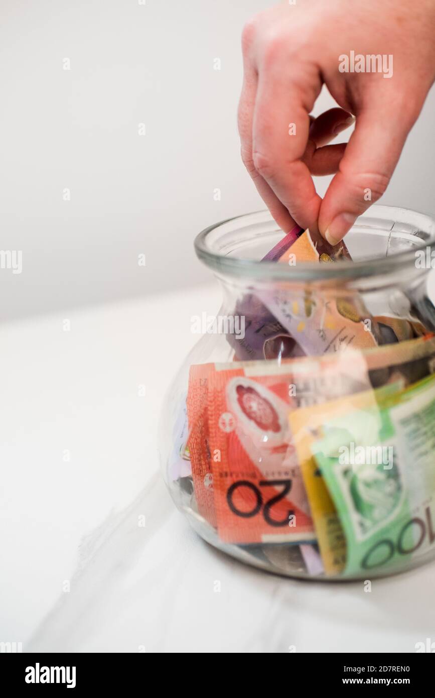 Vertical shot of a hand putting an Australian dollar banknote in a jar ...