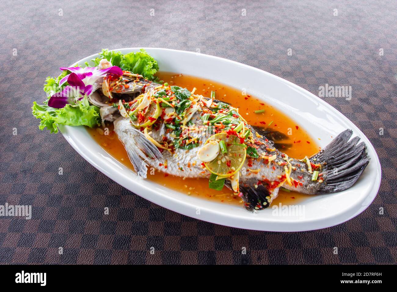 Steamed sea bass fish with lemon put a white ceramic dish on leather ...