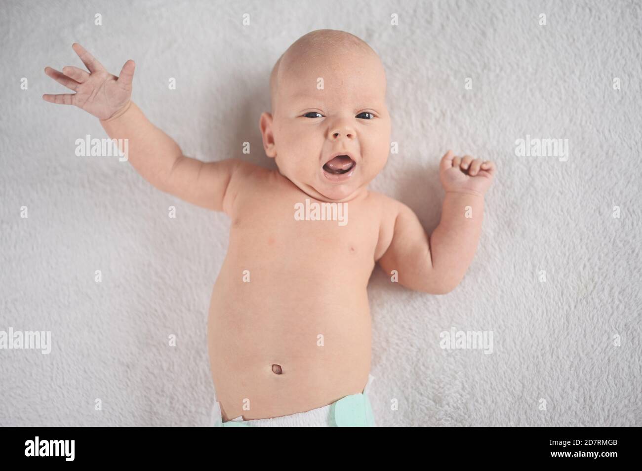 Cute emotional smiling funny newborn boy laying on bed top view. Baby ...