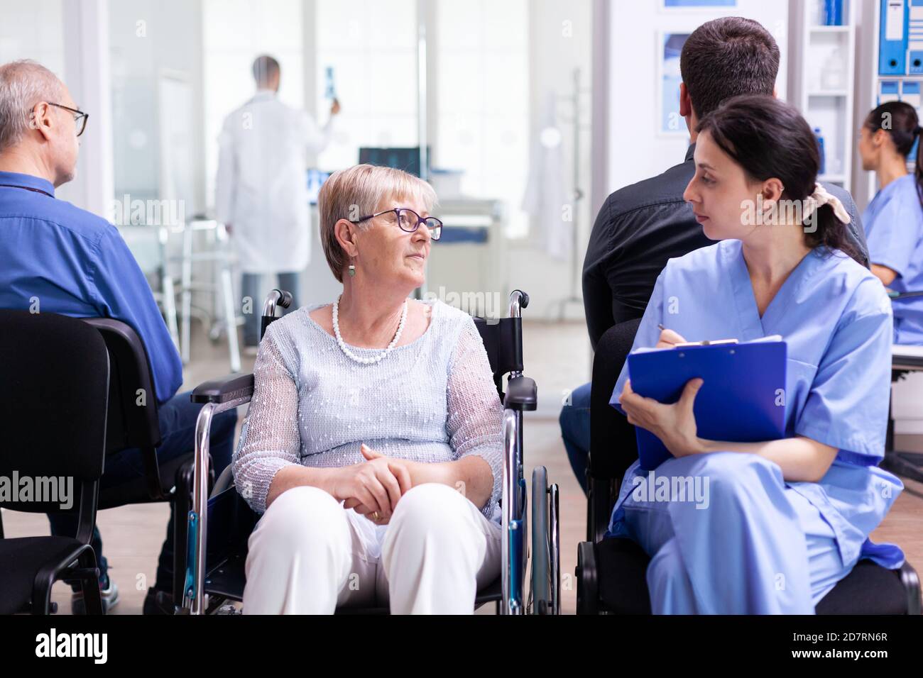 Nurse filing documents while talking with disabled senior woman in ...