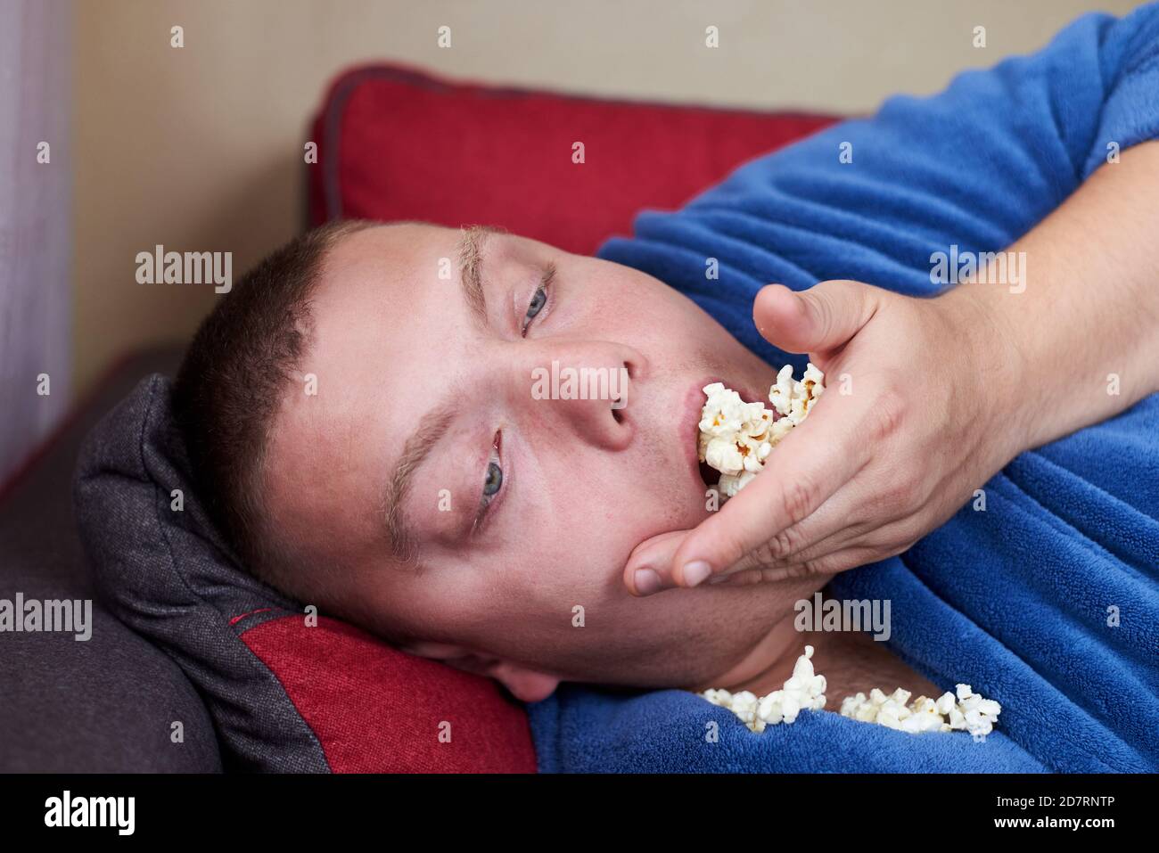 Fat man in a robe eating popcorn while lying on the couch, obesity and ...