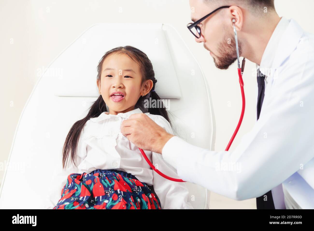 Young male doctor examining little kid in hospital office. The kid is ...