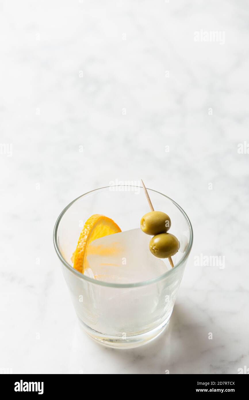 Orange slice, olives and a big ice cube inside a glass. Vermouth ...