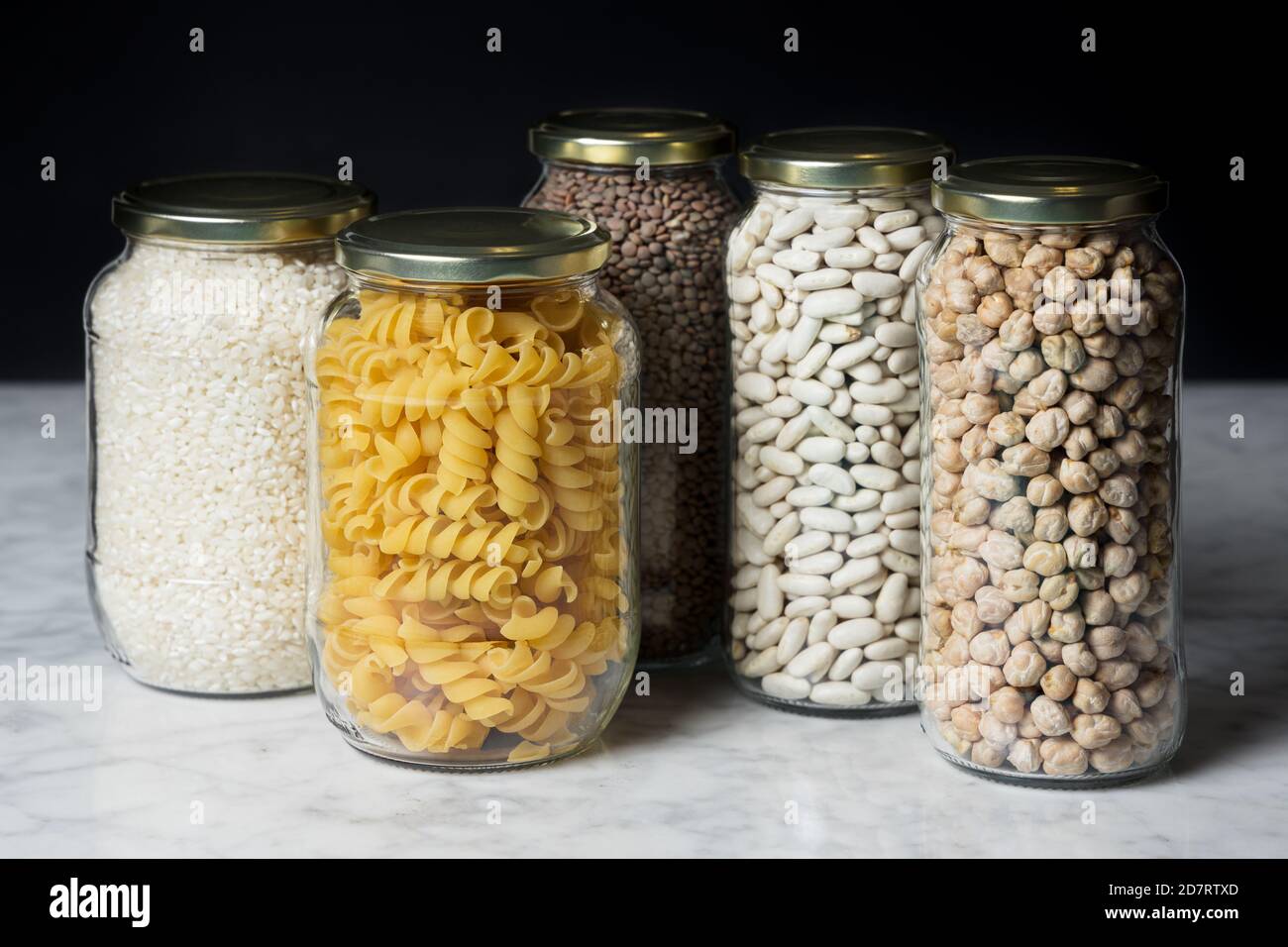 Set of glass jars with various ingredients placed on a marble tabletop ...
