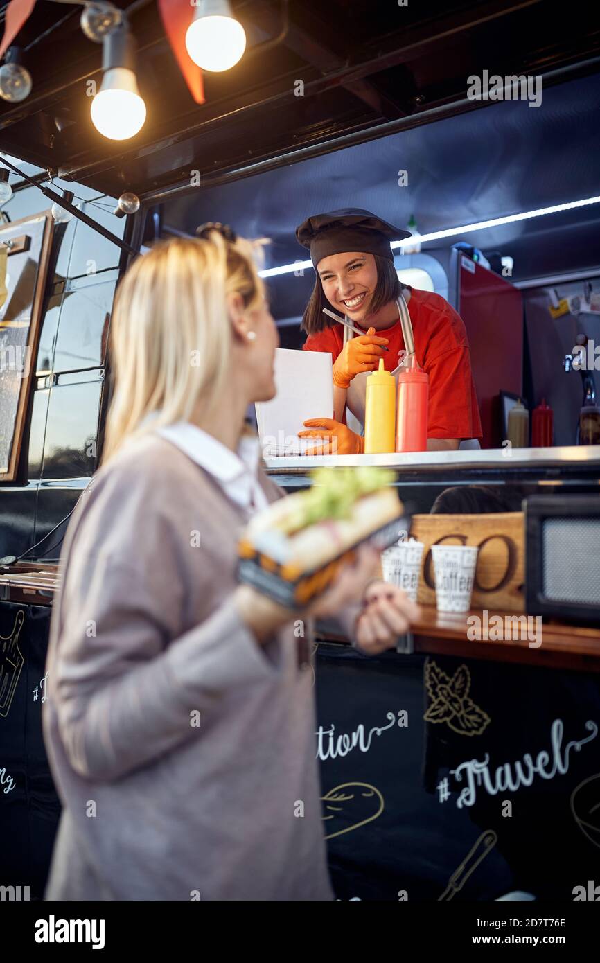 vertical image of a customer with sandwich in hands talking to an ...