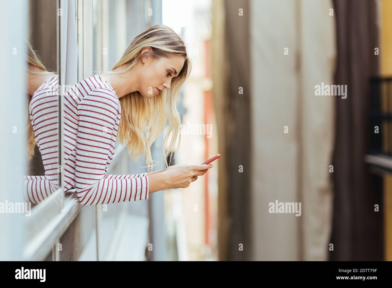 Attractive woman leaning out of her house window using a smartphone ...