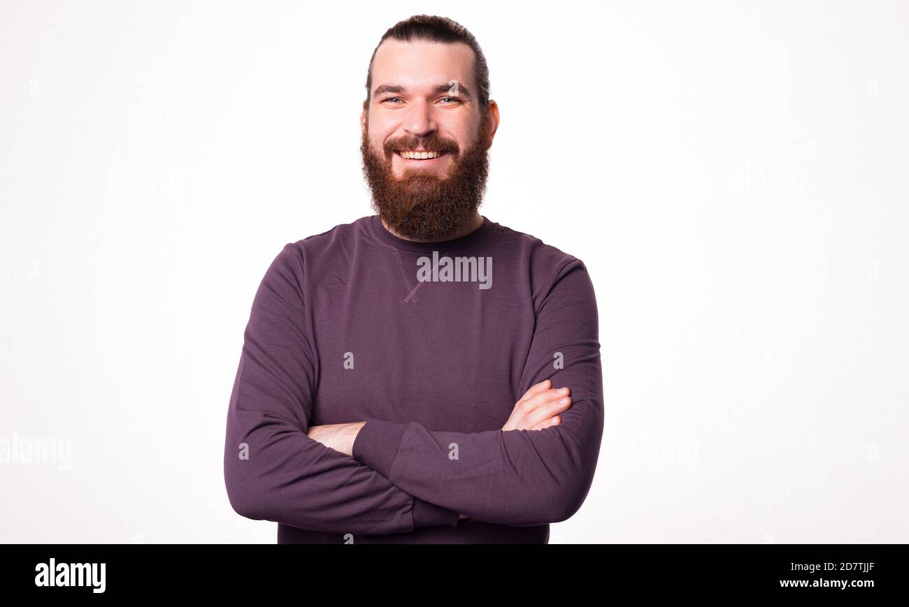 Bearded man is smiling at the camera and sitting with his arms crossed ...