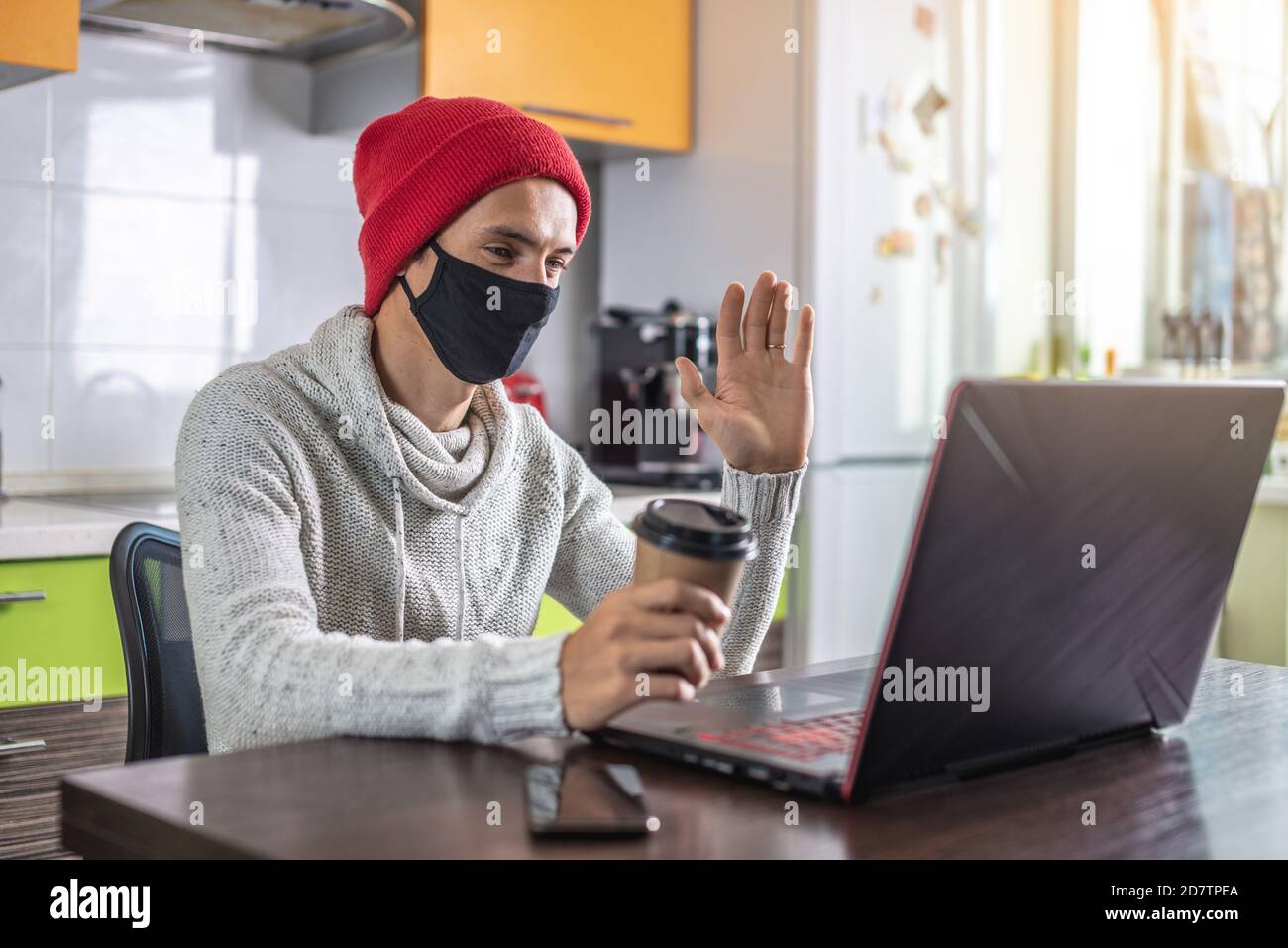 A young man in a protective face mask is looking at the laptop screen ...