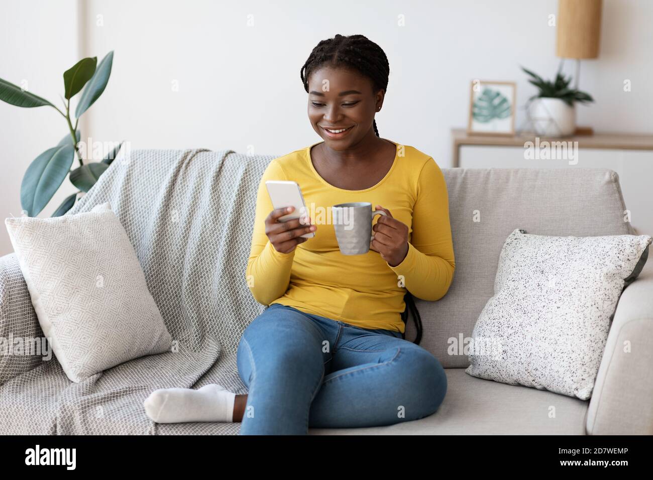 Domestic Relax. Positive black lady resting on couch with smartphone ...
