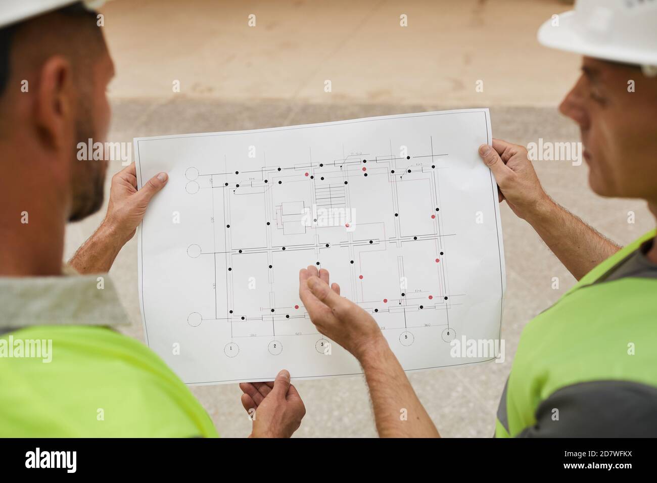 Back view at two building contractors looking at plans while standing ...