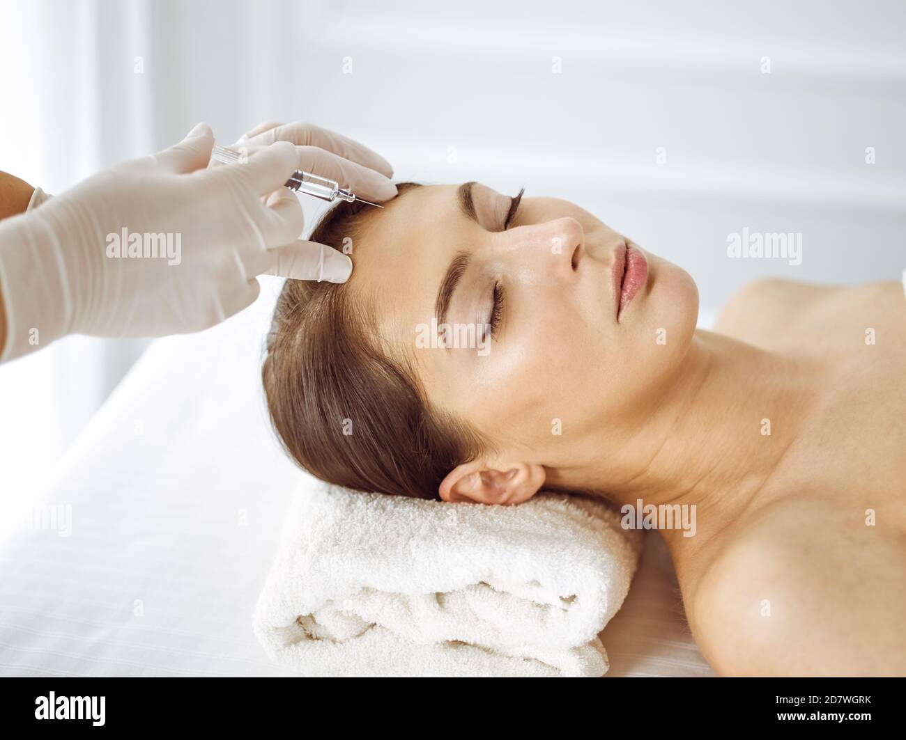 Beautician doing beauty procedure with syringe to face of young brunette woman. Cosmetic ...