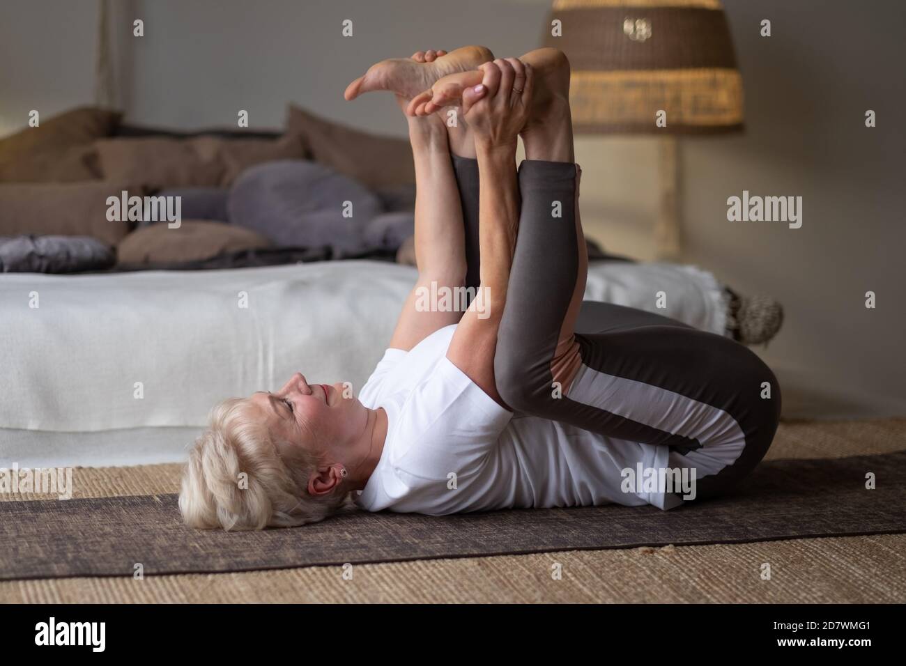 Senior woman doing yoga in sunny room. Happy Baby Pose Stock Photo - Alamy