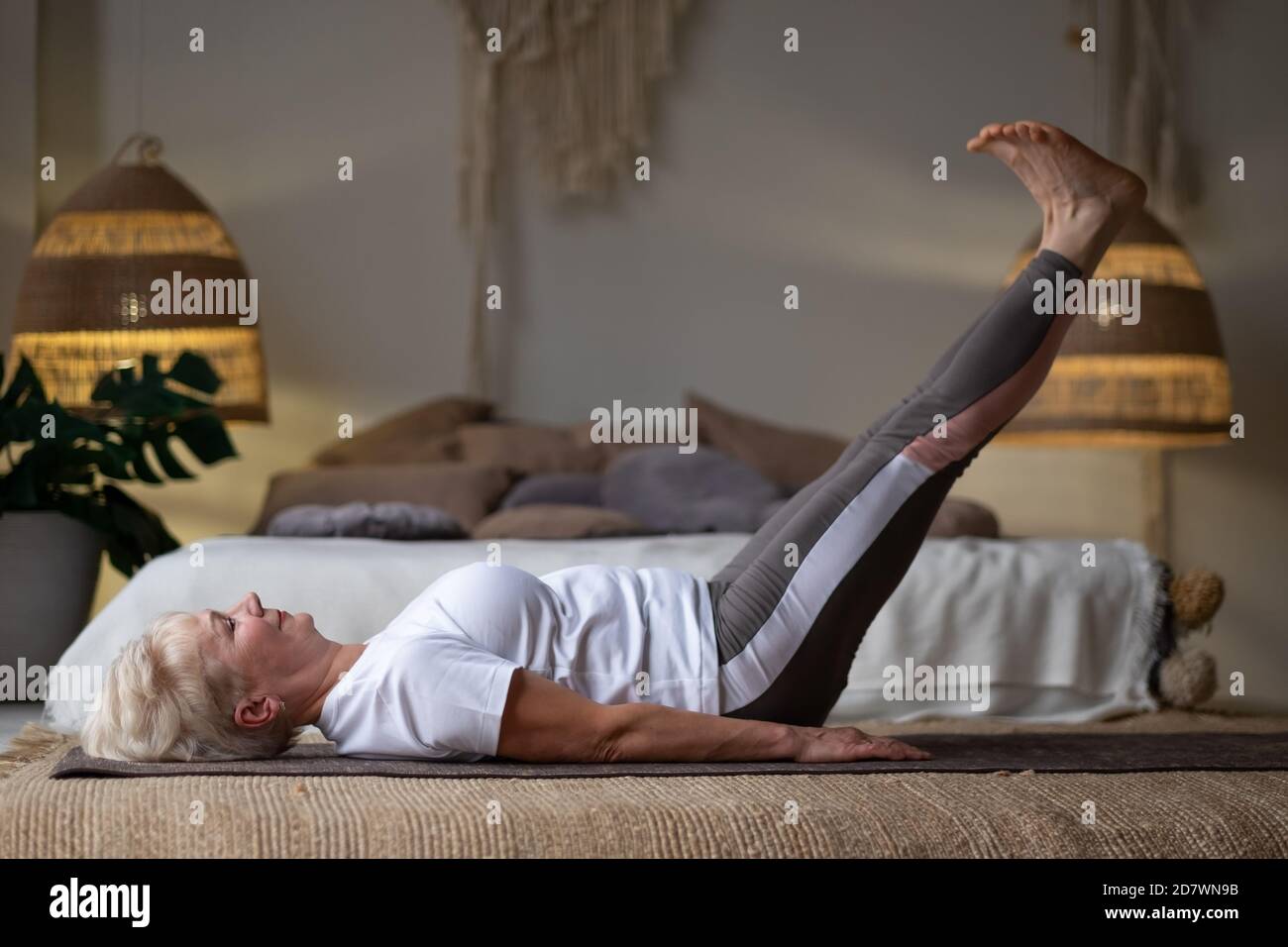 Senior woman lying on mat with legs up at home Stock Photo - Alamy