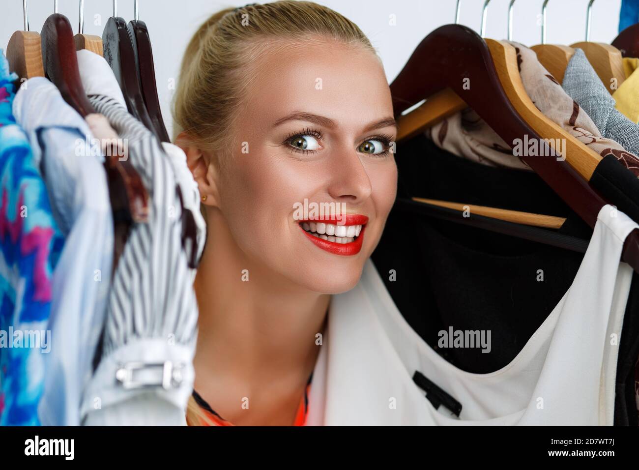 Beautiful smiling blonde woman standing inside wardrobe rack full of ...