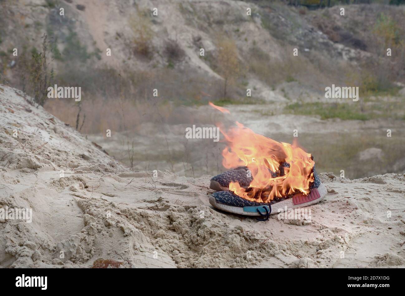 Burning sports sneakers or gym shoes on fire stand on sandy beach coast ...