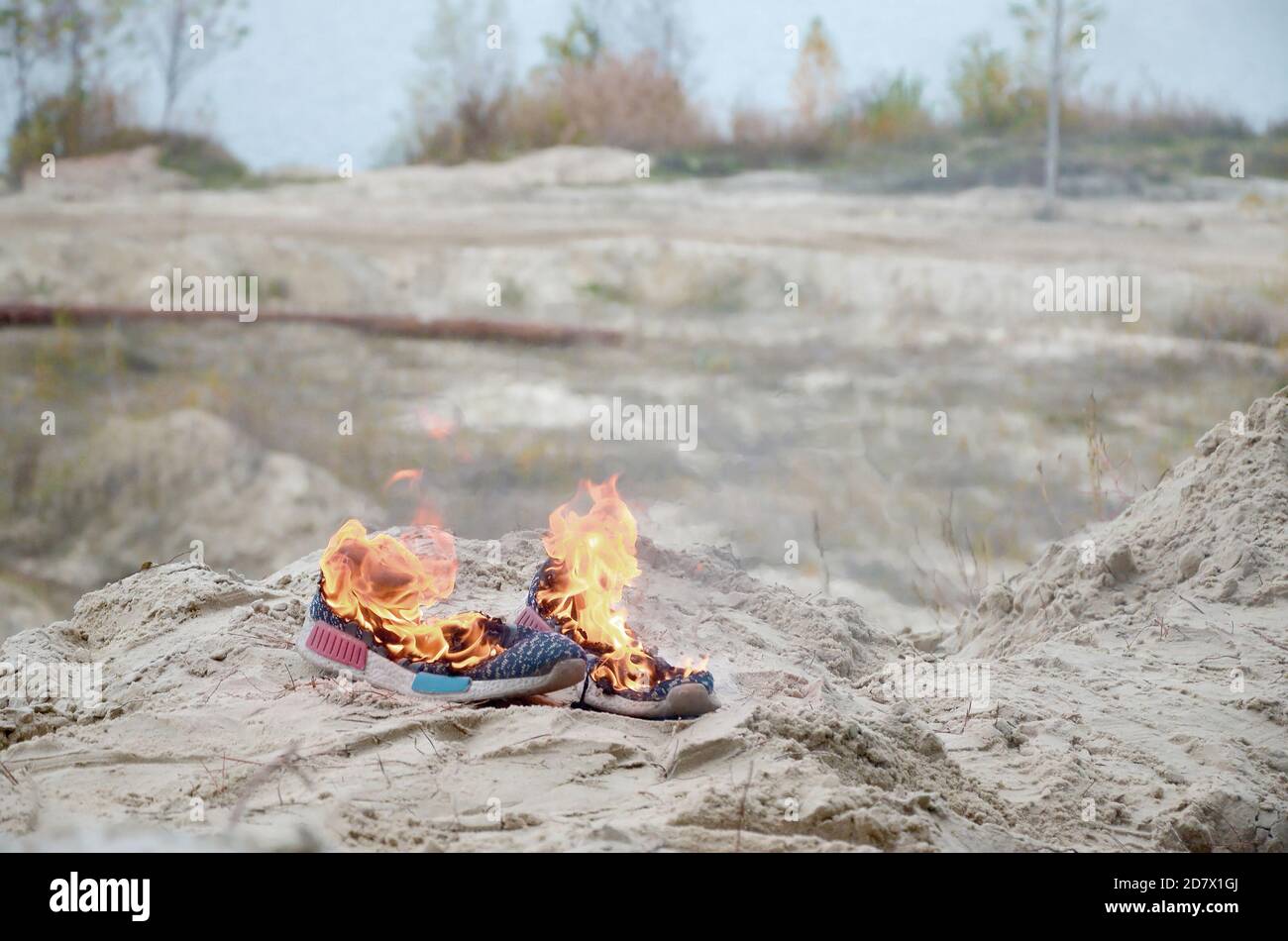 Burning sports sneakers or gym shoes on fire stand on sandy beach coast ...