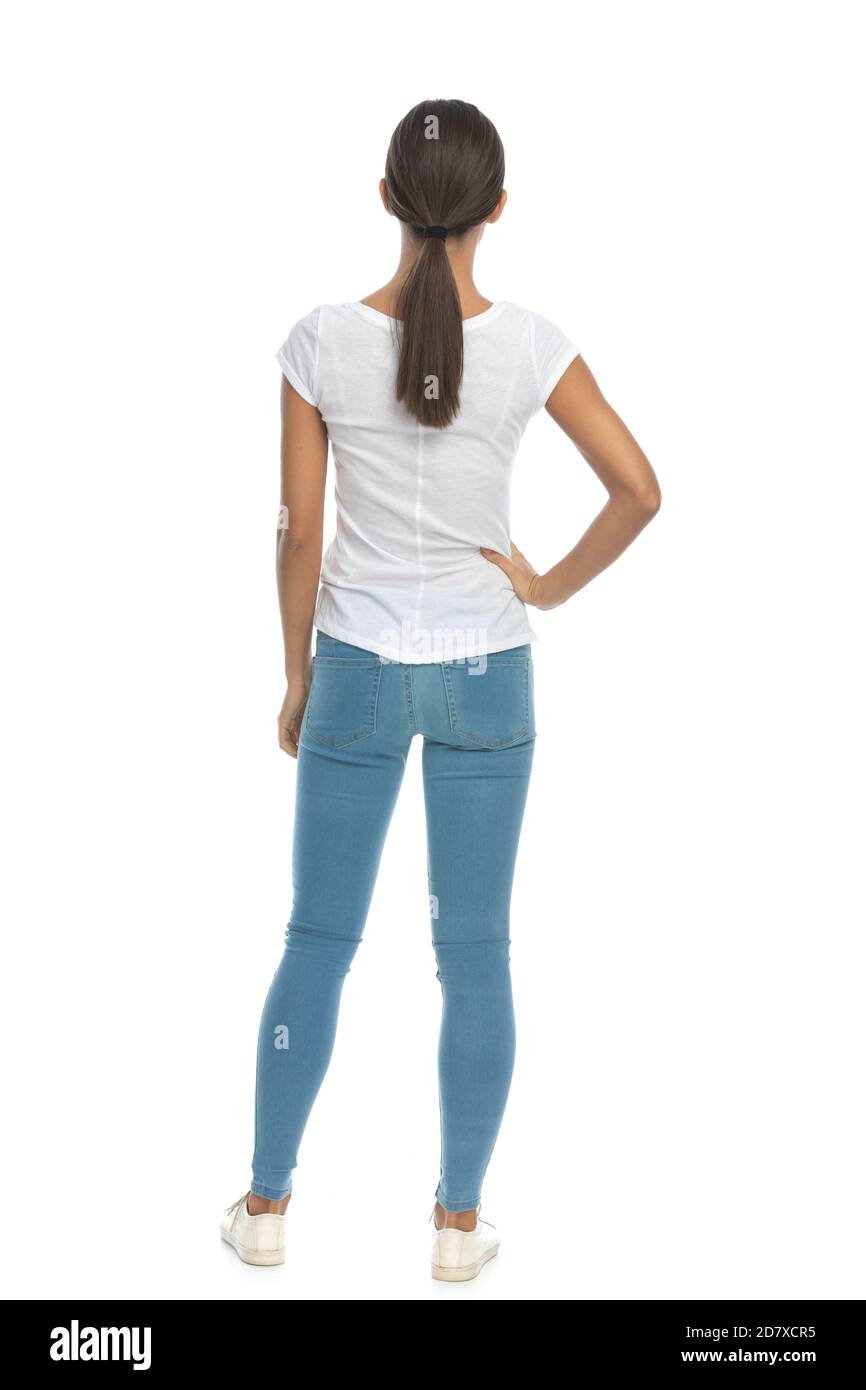 Back view of casual woman holding hand oh hip while standing on white ...
