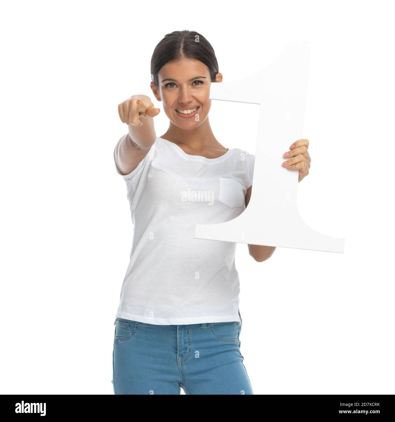 Positive casual woman holding number one and pointing while standing on ...