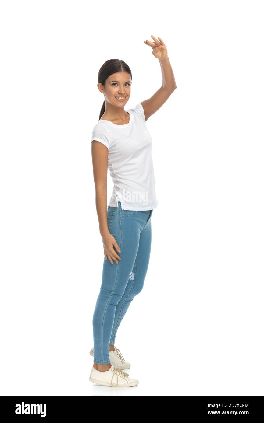 Side view of casual woman smiling and waving, standing on white studio ...