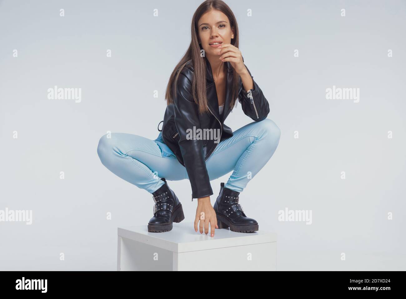 Positive fashion model smiling, wearing leather jacket while crouching ...