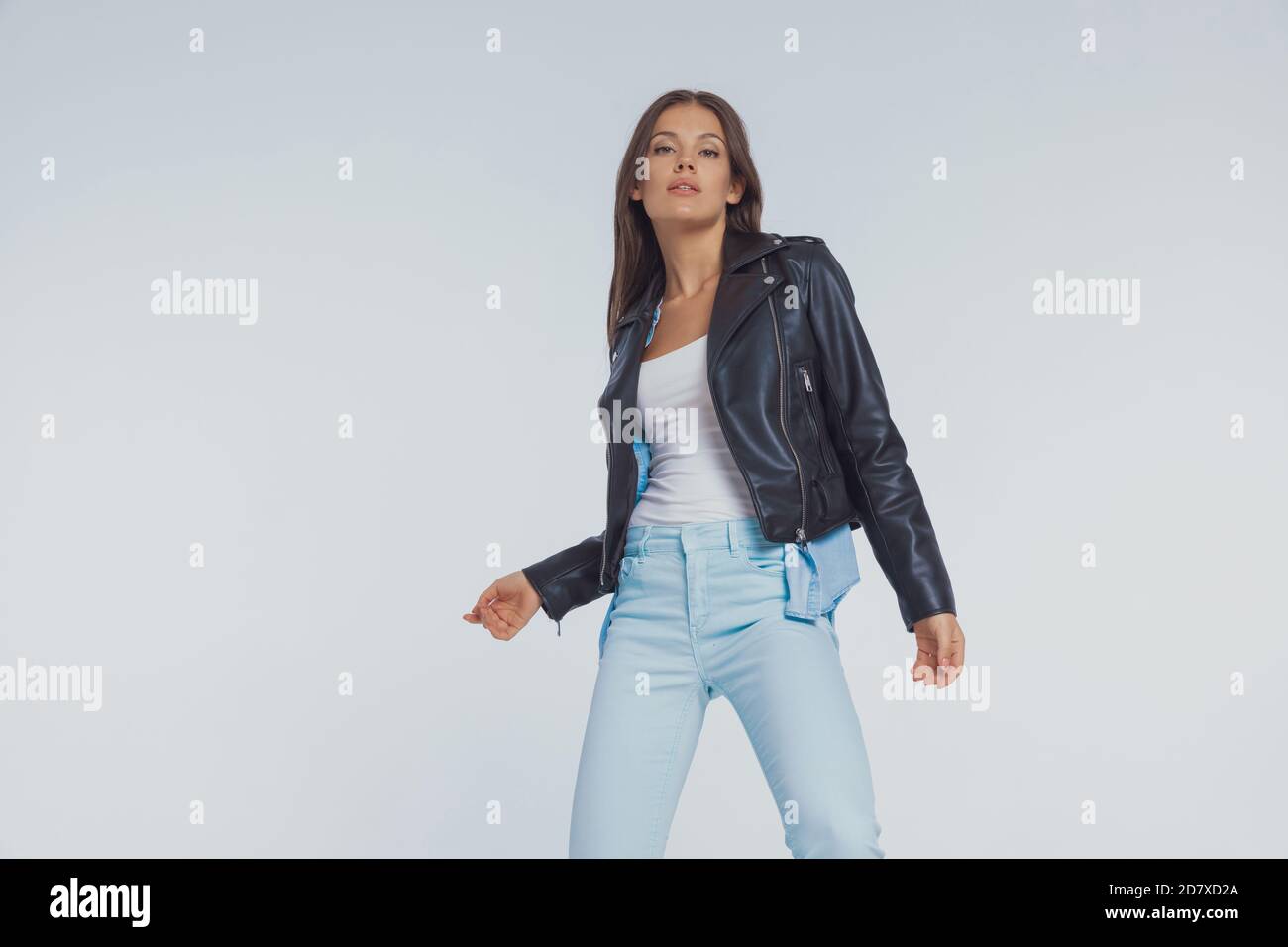 Charming fashion model wearing leather jacket while standing on gray ...