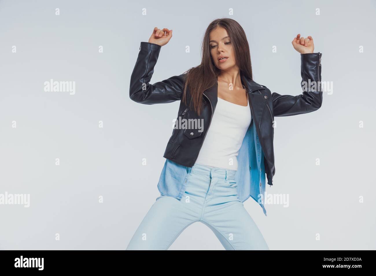 Confident fashion model wearing leather jacket and dancing on gray ...