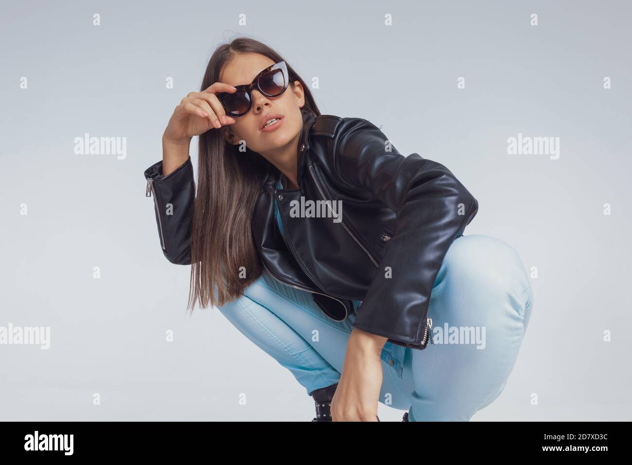 Young fashion model adjusting sunglasses while wearing leather jacket ...