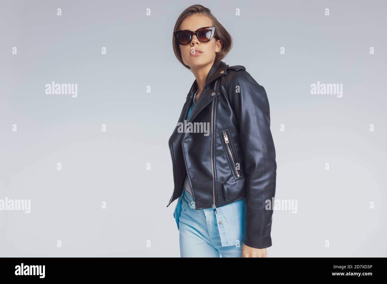 Serious fashion model wearing leather jacket and sunglasses, standing ...