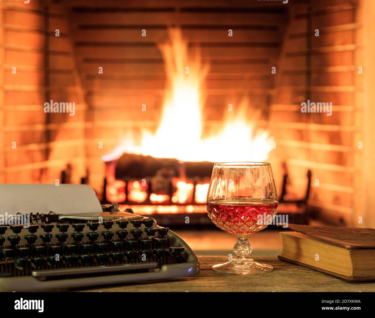 Glass of brandy and a typewriter on burning fireplace background. Warm ...