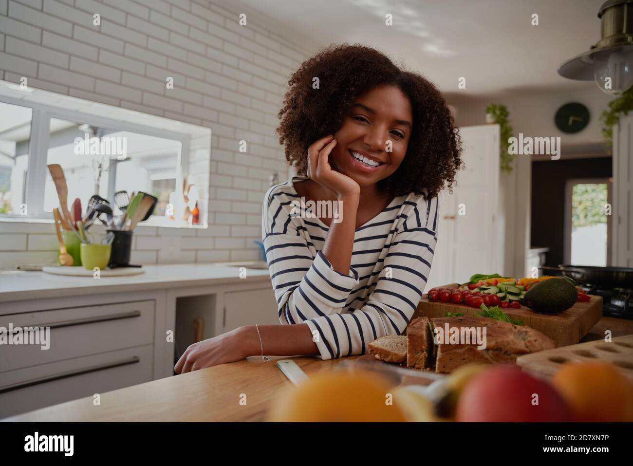 Young woman leaning on modern kitchen counter with chopped vegetables ...