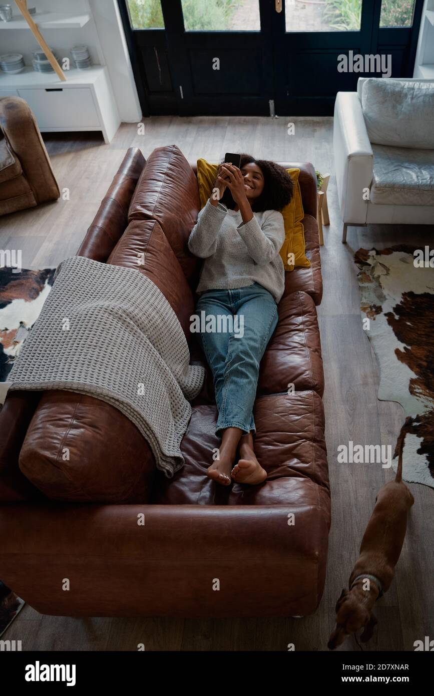 High angle view of woman sleeping on sofa barefoot listening to music ...
