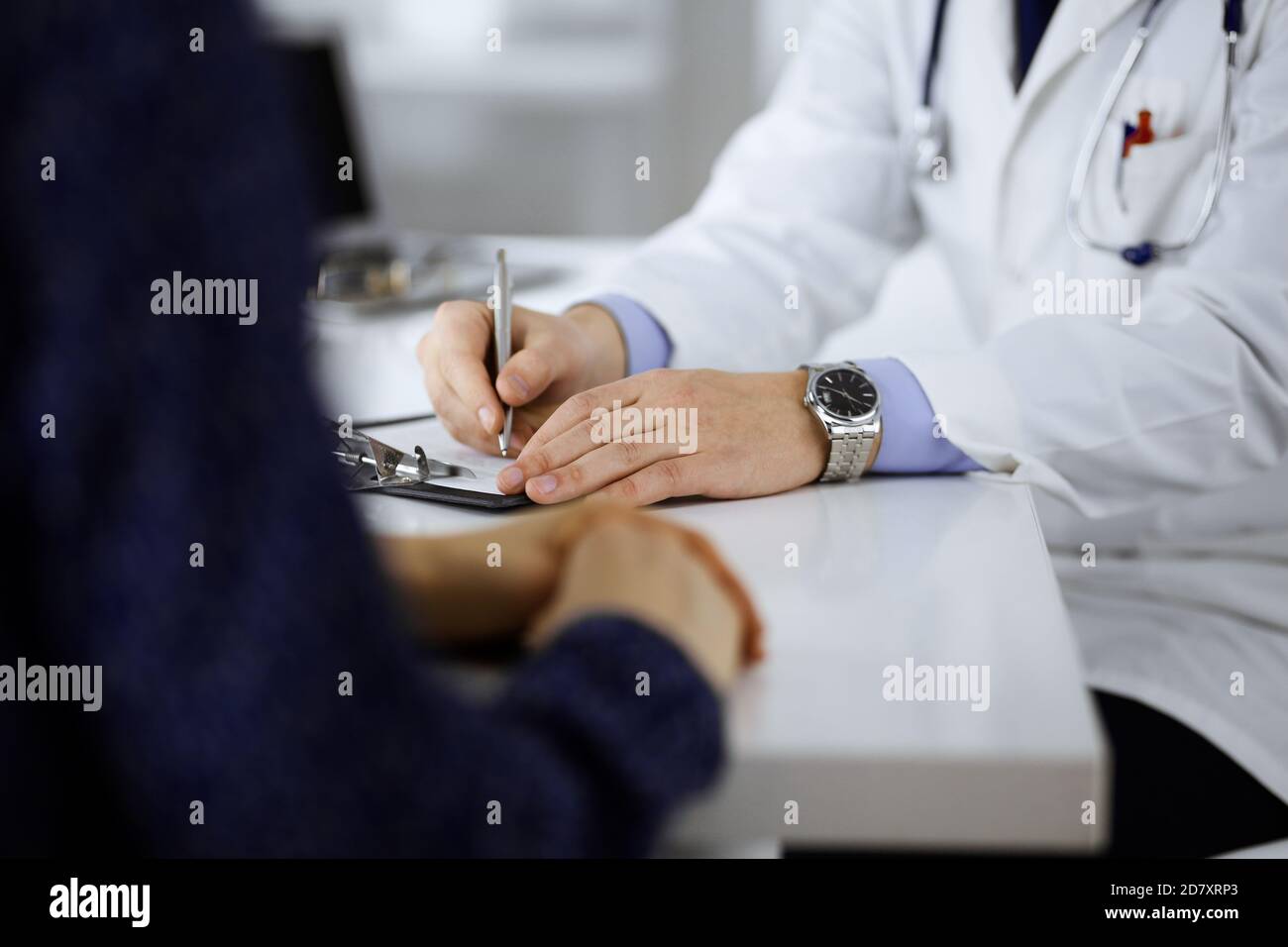 Unknown doctor is writing a receipt for his patient, sitting in his ...