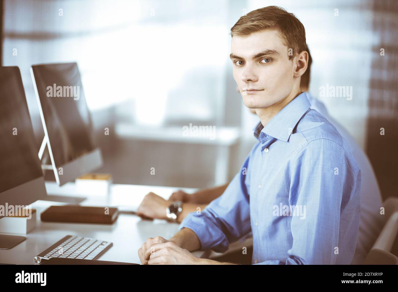 Two young confident businessmen, sitting at the desk in a modern office ...