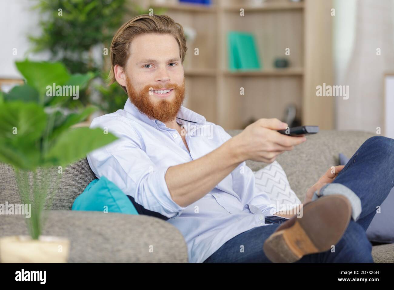 contented man on the sofa using tv remote control Stock Photo - Alamy