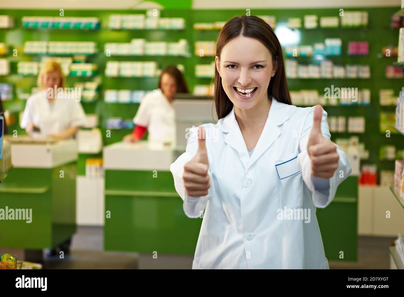 Laughing pharmacist in pharmacy holds both thumbs up Stock Photo - Alamy
