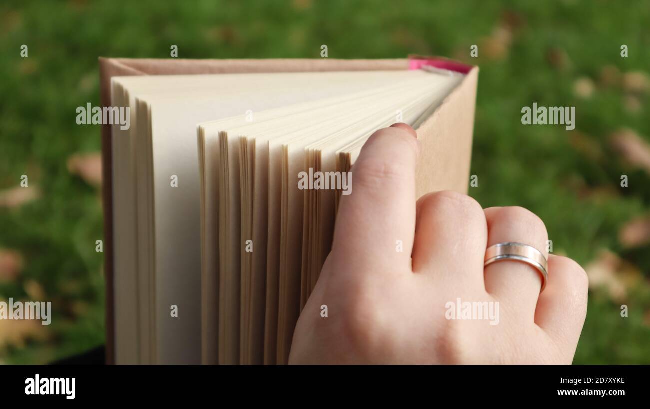 Girl reading a book in the autumn park. Female hands open the pages of ...