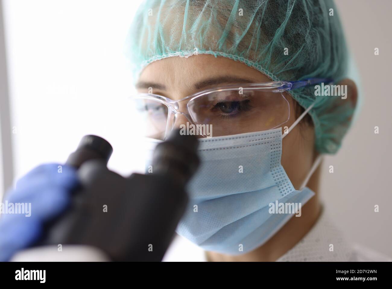 Researcher wearing mask and glasses looks through microscope Stock ...