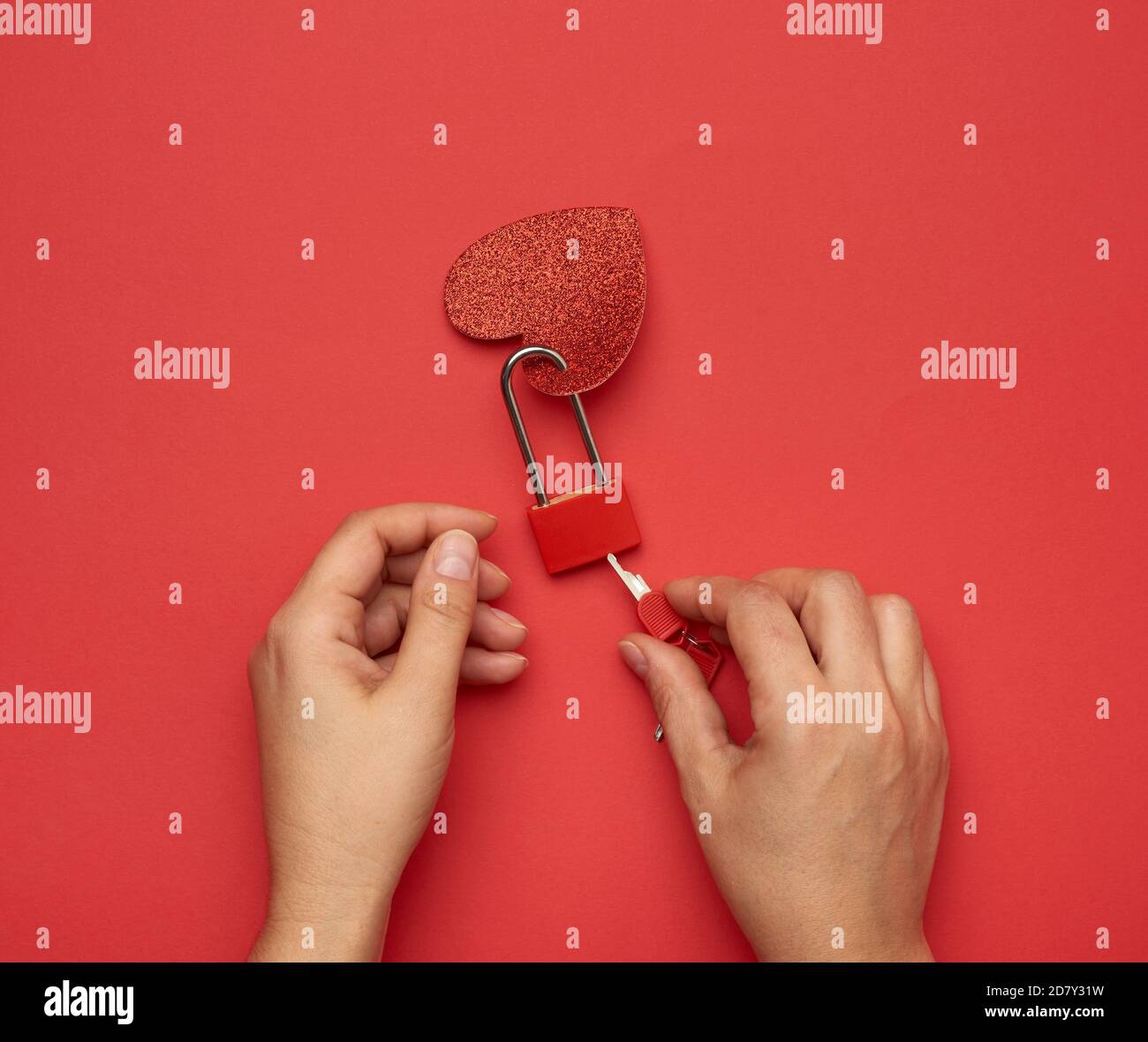 two female hands hold a metal lock and keys on a red background, top ...