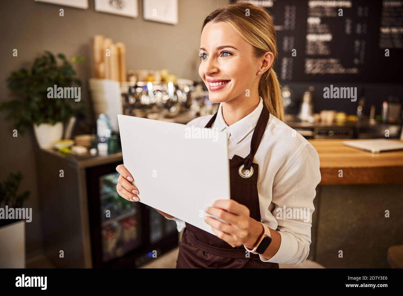 Happy coffeehouse waiter in aprons holding white paper in hand Stock ...