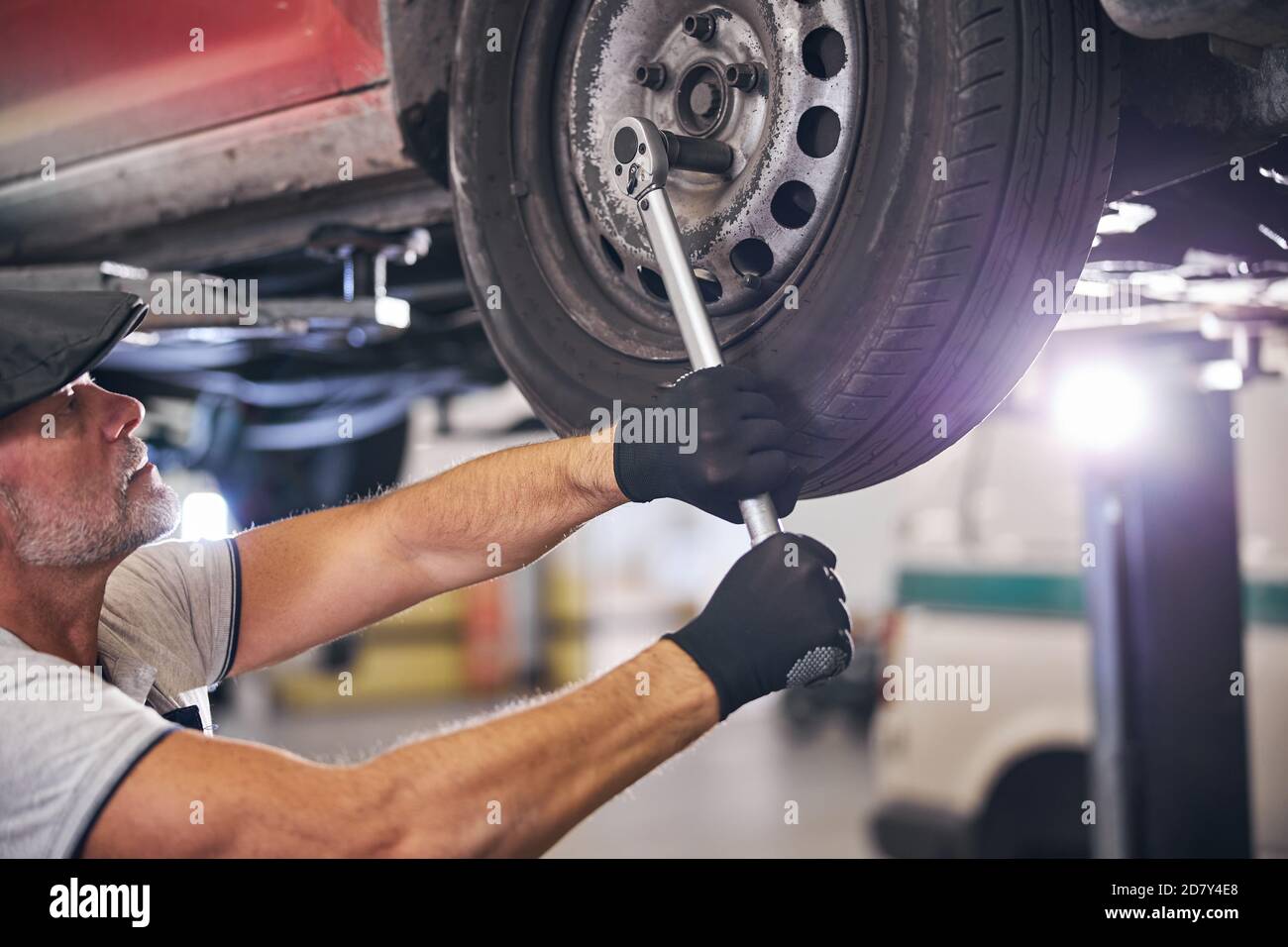 Bearded male technician repairing car wheel at auto service station ...